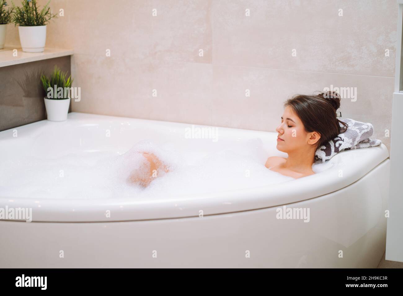Young woman lies in white bath of foam with her eyes closed. Spa procedures, cleansing ...