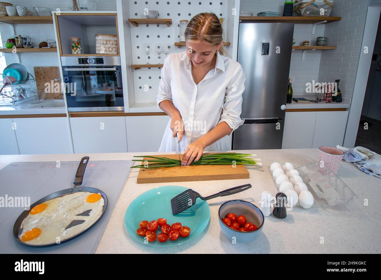 Beautiful young woman cooking in a modern kitchen. Slicing spring onion ...