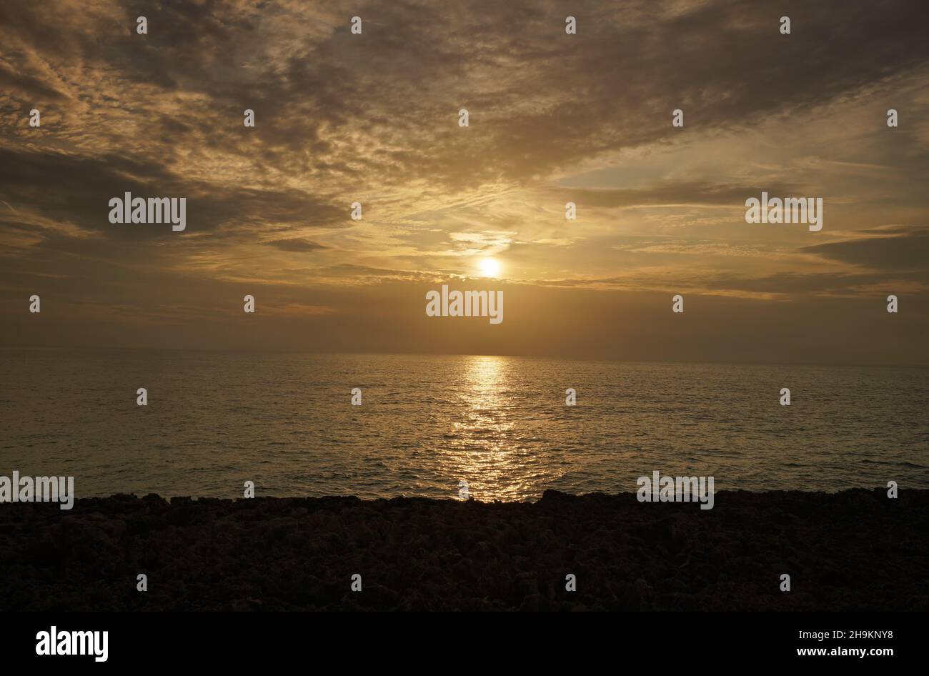 Sun rising above sea, clouds lit by yellow light Stock Photo - Alamy