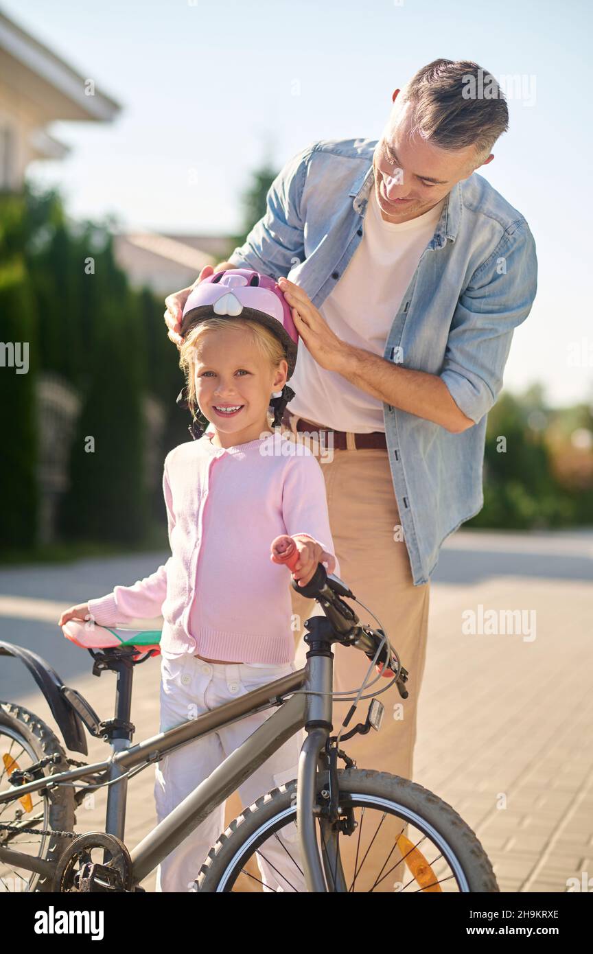 A man putting protective helmet on his daughters head before riding a ...