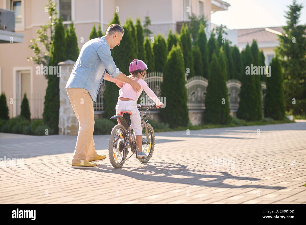 Dad helping his daughter learn riding a bike Stock Photo - Alamy