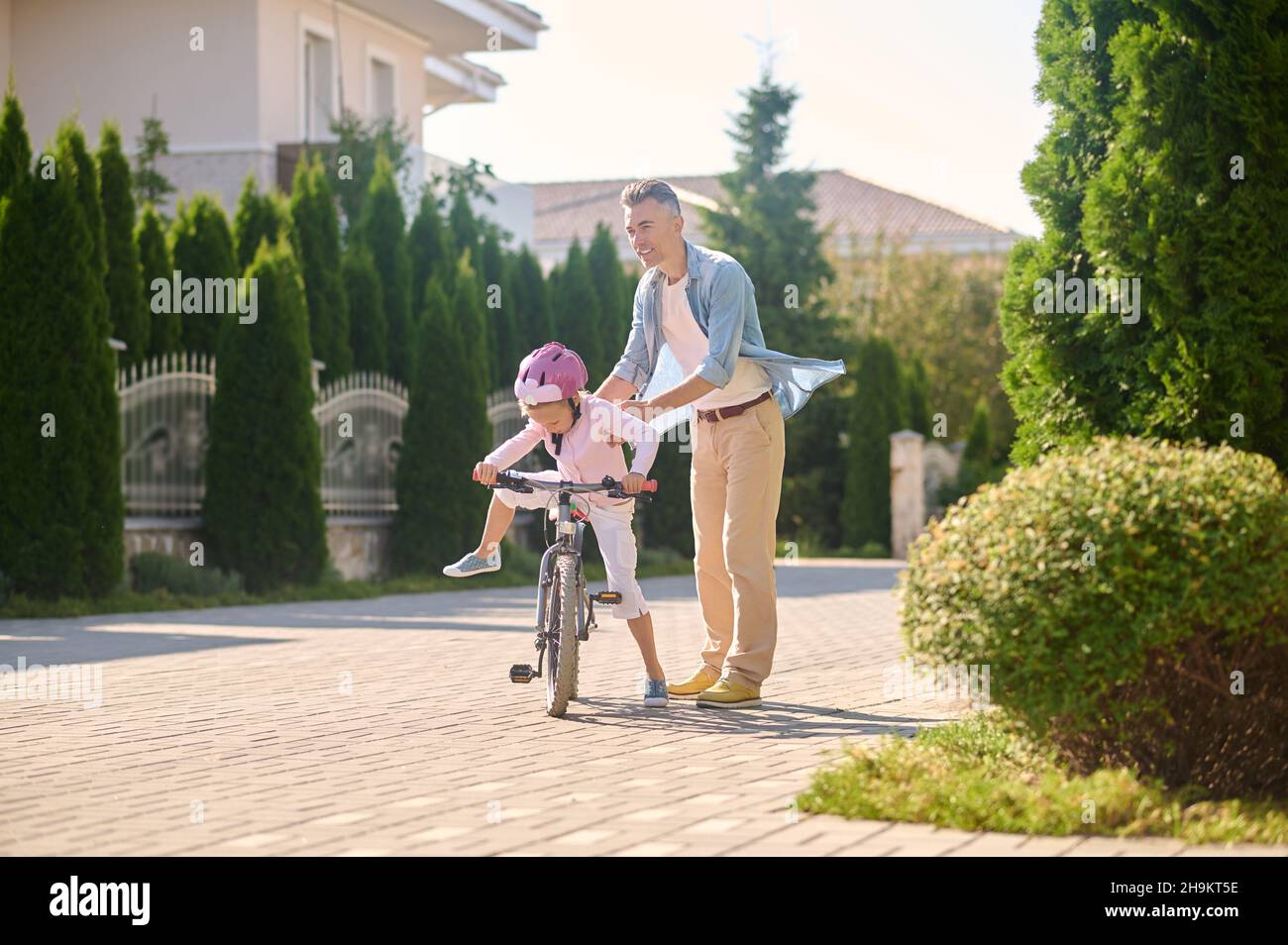 Dad helping his daughter learn riding a bike Stock Photo - Alamy