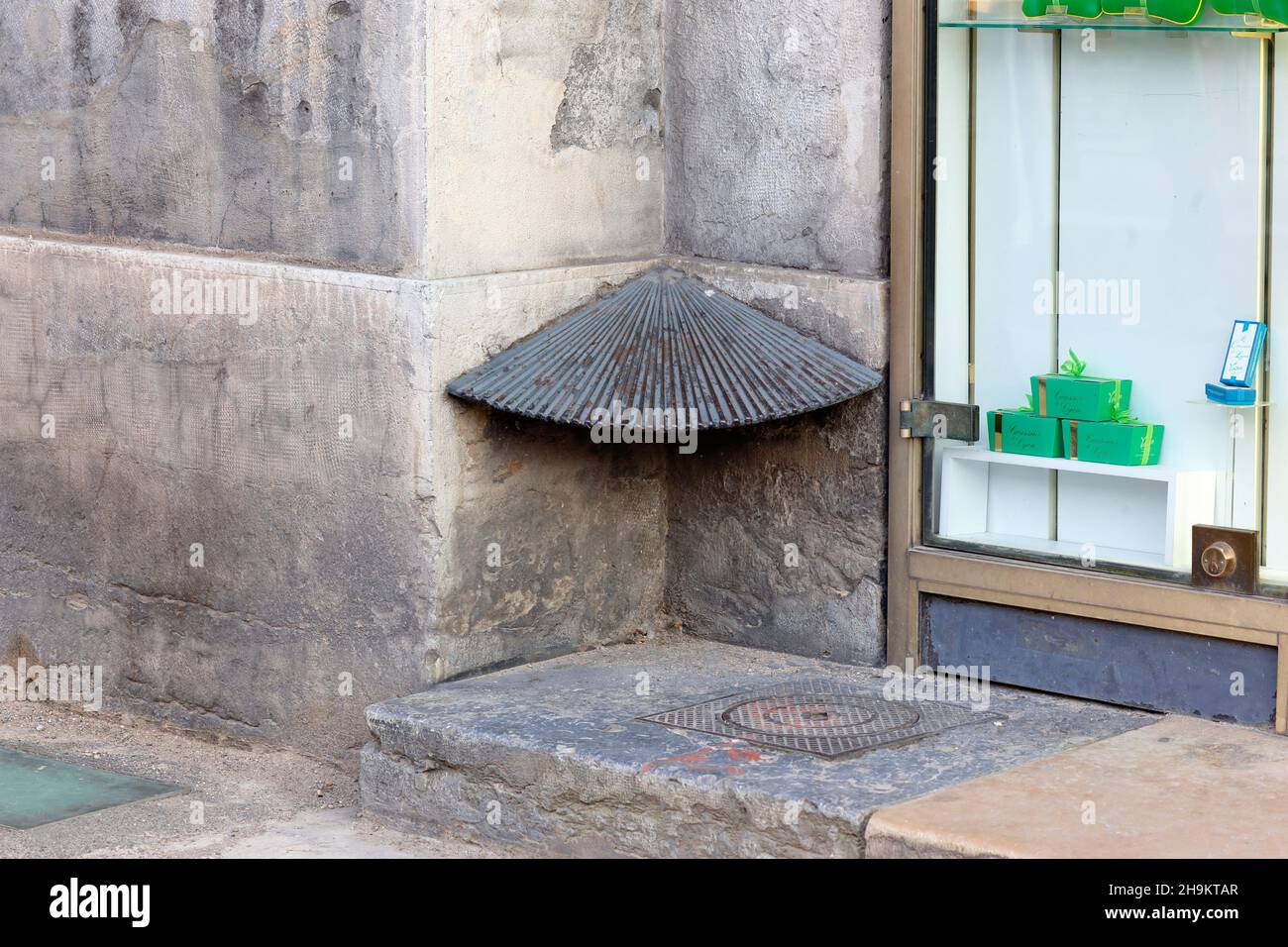 A scalloped, beaux-arts urine deflector installed on a corner of the ...