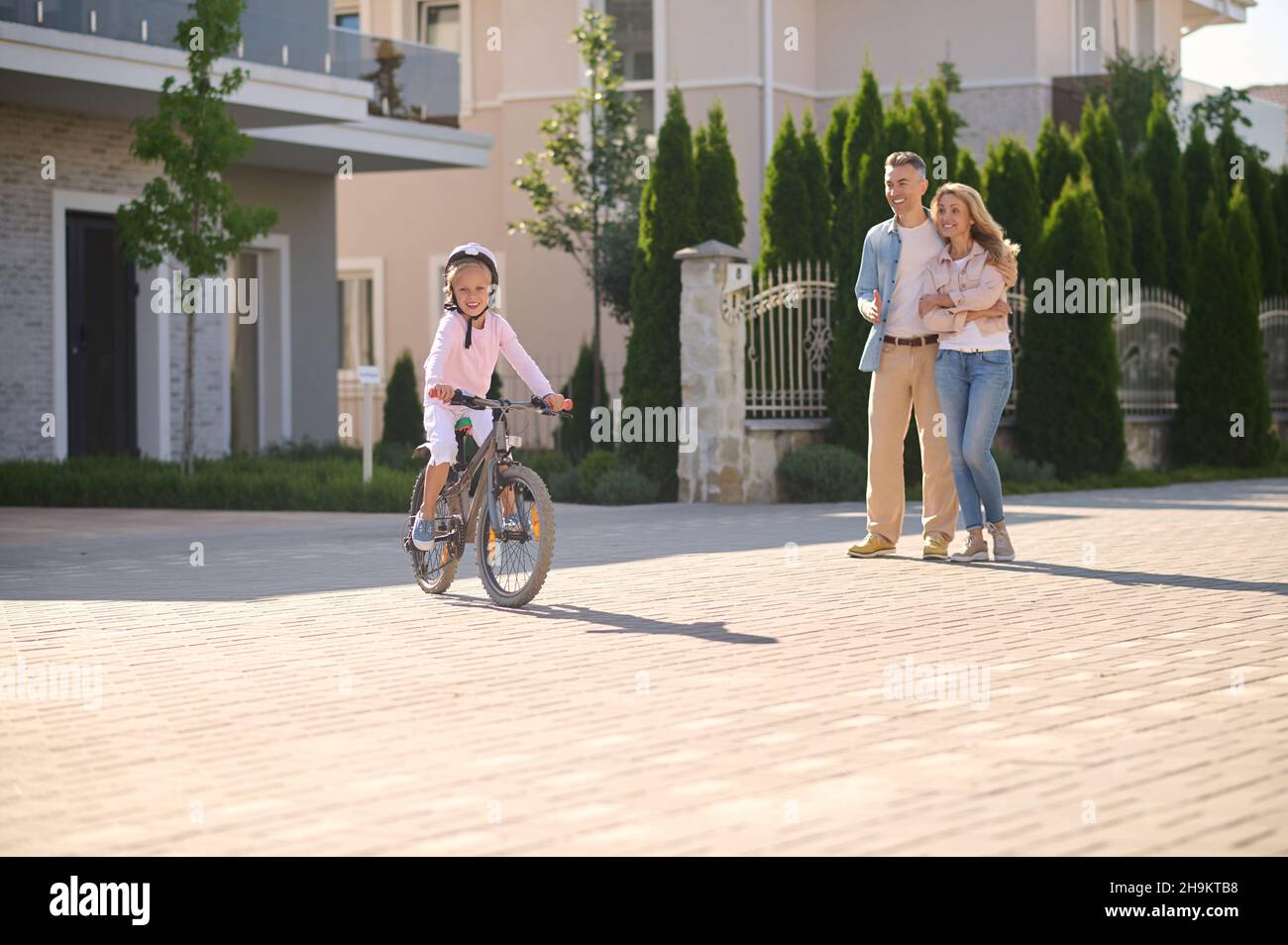 A girl riding a bike while her parents watching her Stock Photo - Alamy