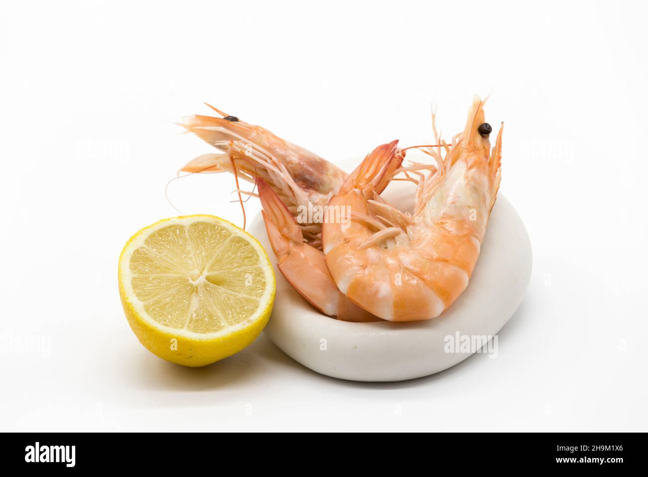 two prawns in a small container and half a lemon, all on white ...