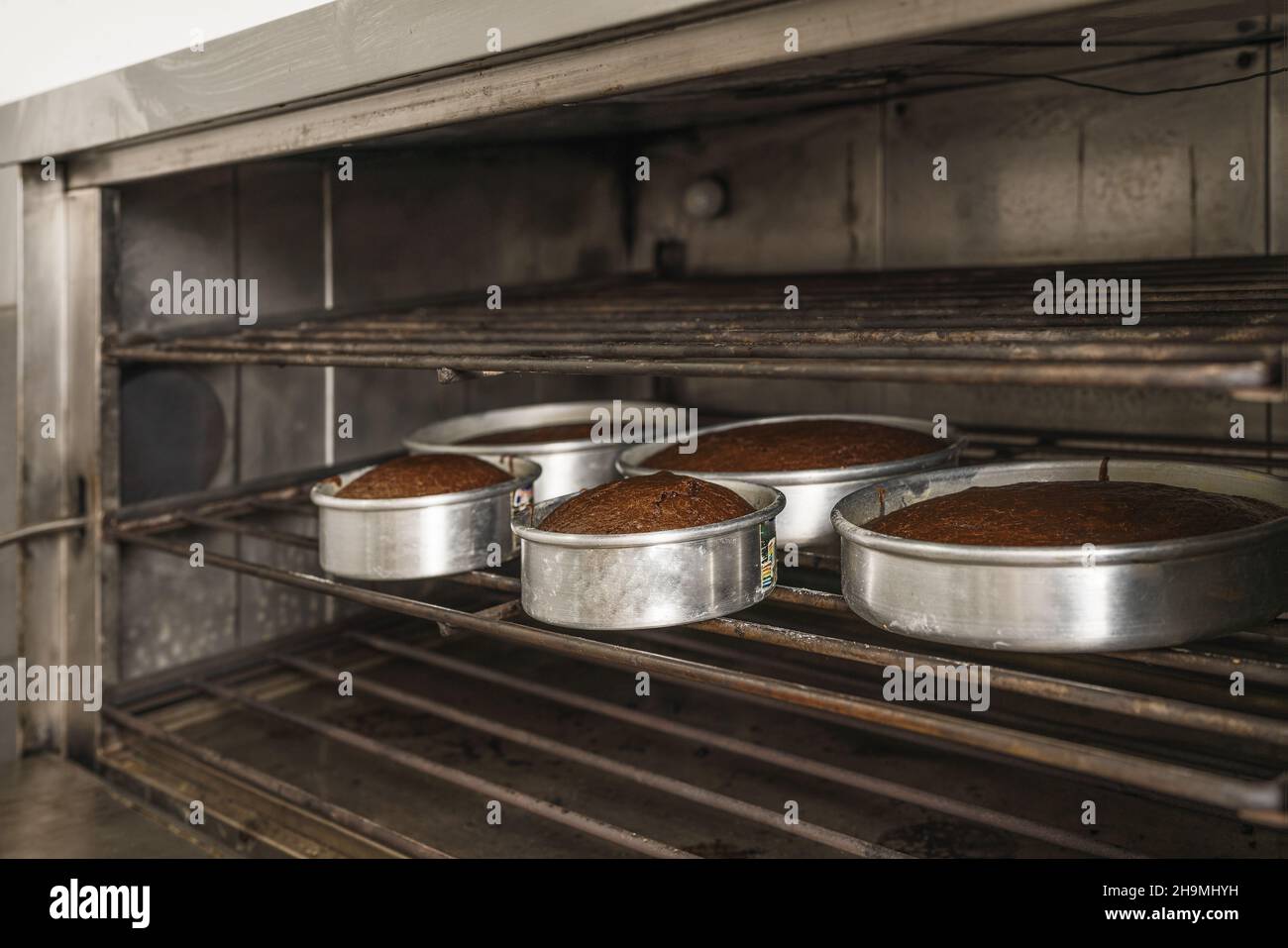 Five round cakes in a silver container into an industrial oven in a ...