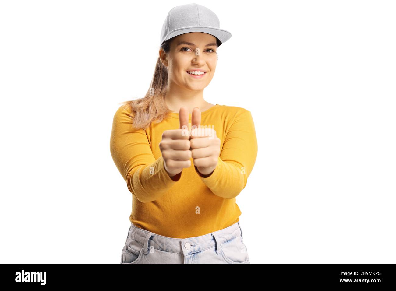 Cheerful young female with a yellow top and cap gesturing thumbs up ...