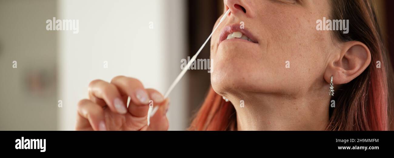 Wide view image of a young woman swabing her nose with a testing stick ...