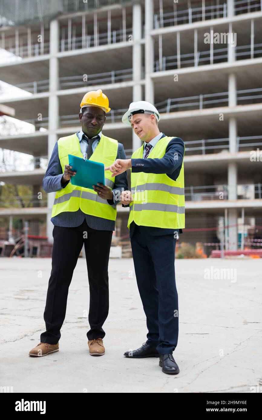 Two civil engineers are discussing the construction plan, holding ...