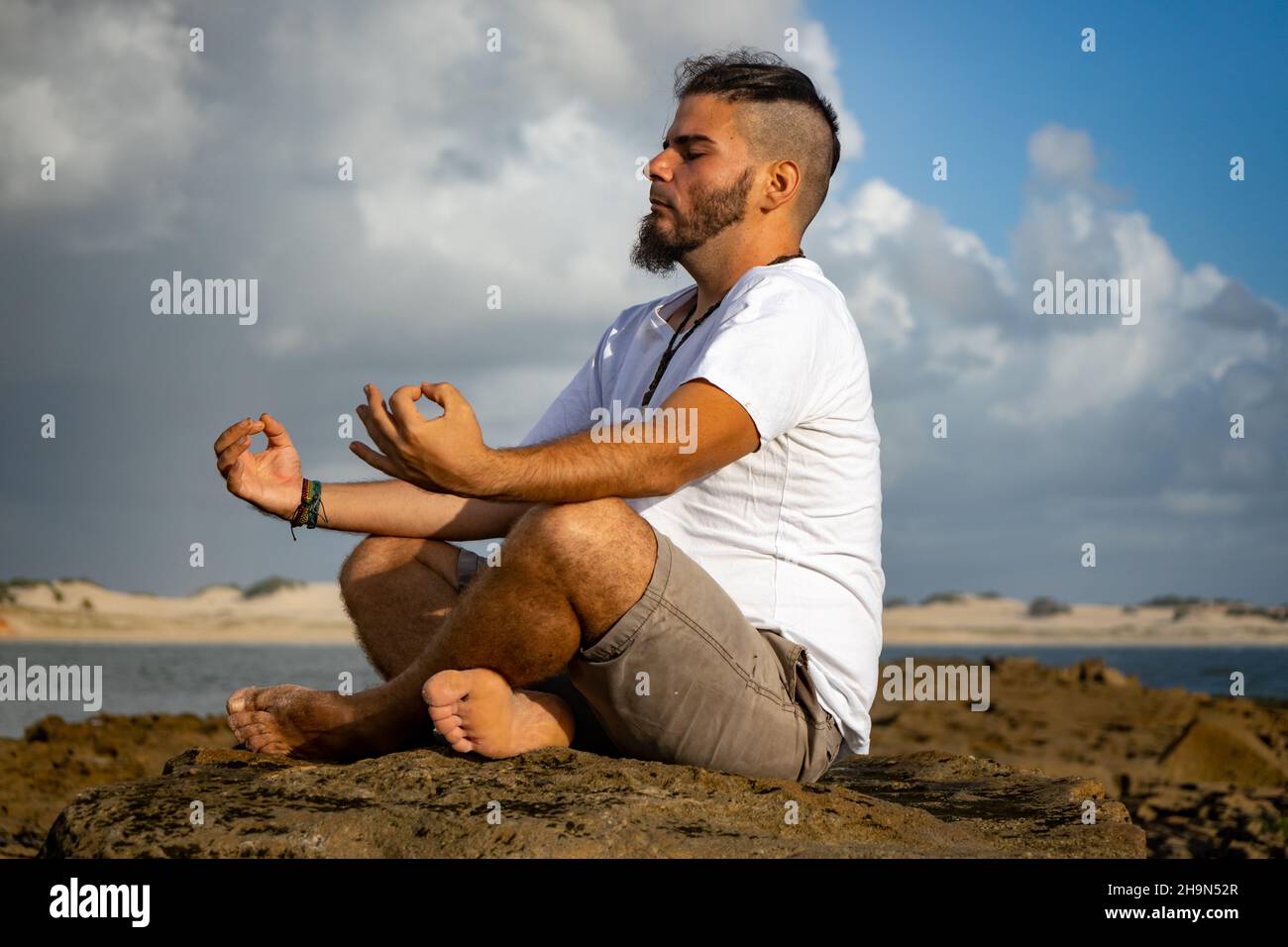 Young man of hippie appearance doing yoga on a beach. Introspective and ...