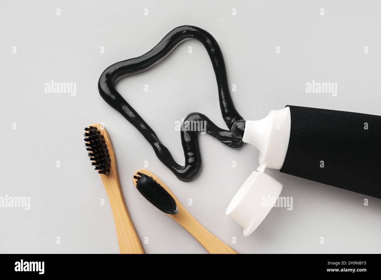 Tooth made of black paste, bamboo brushes and tube on light background ...