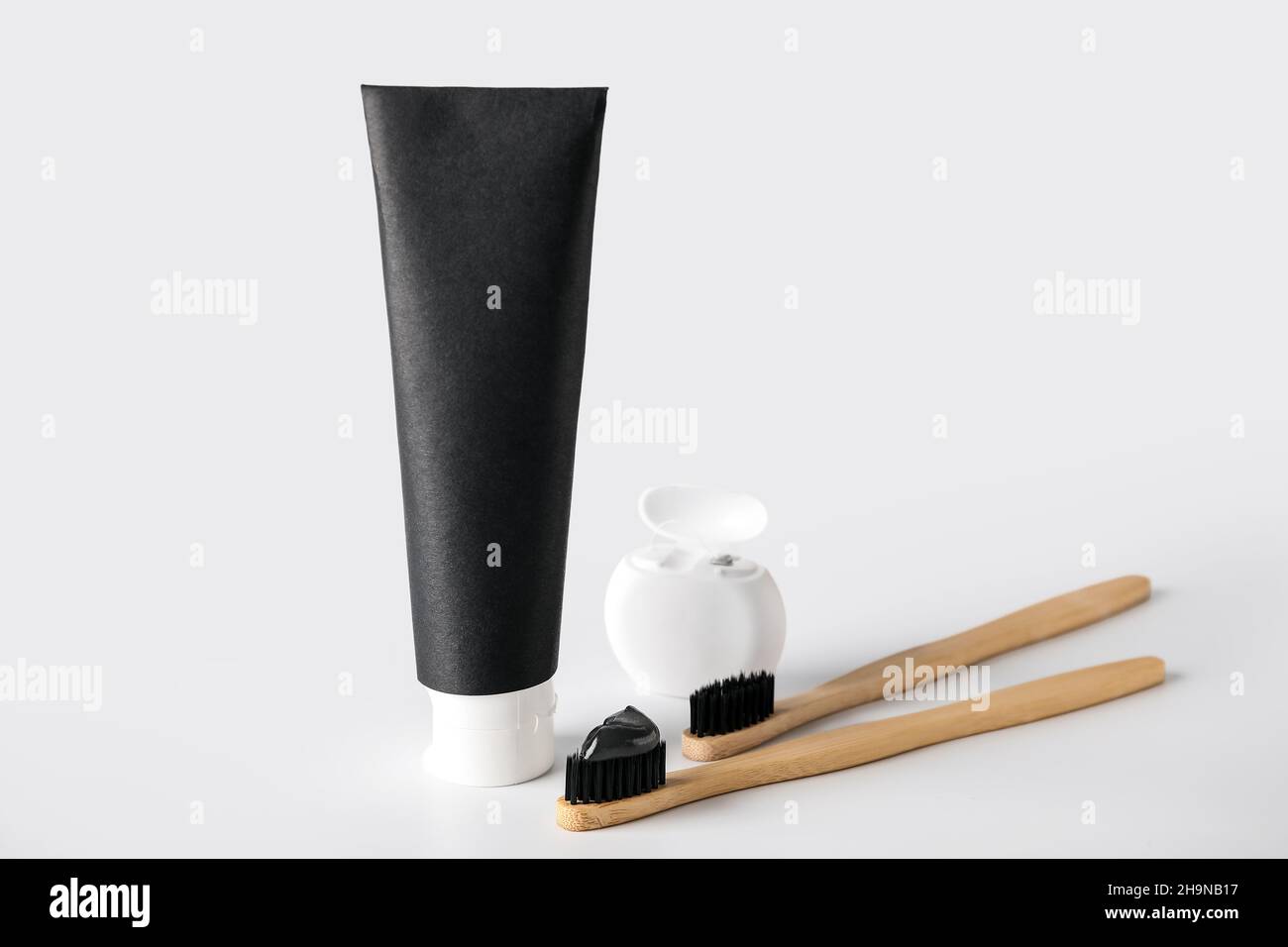 Tube of black tooth paste, bamboo brushes and dental floss on white ...