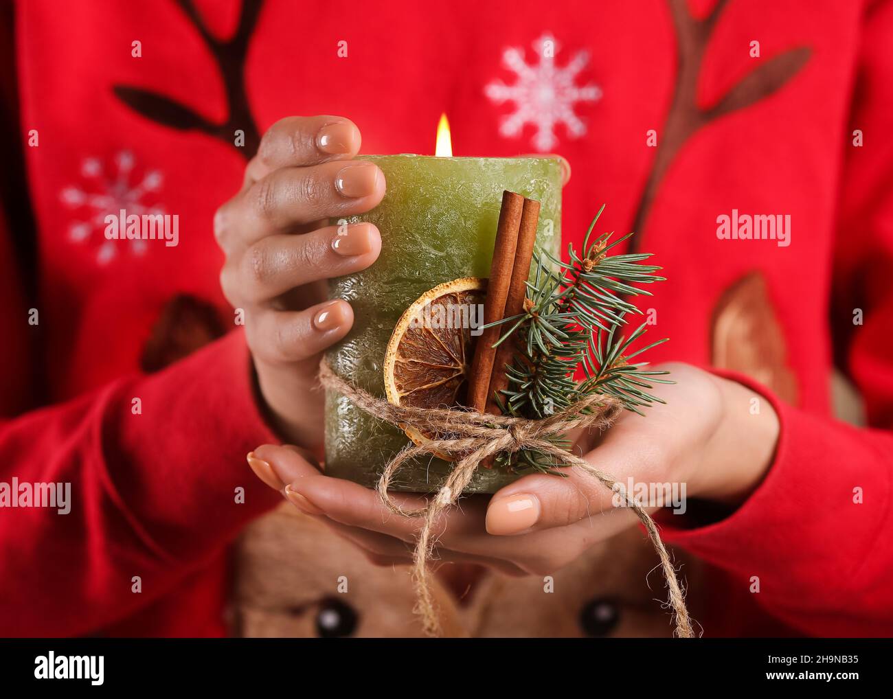 Woman in red sweater holding burning candle with fir branches, dried ...