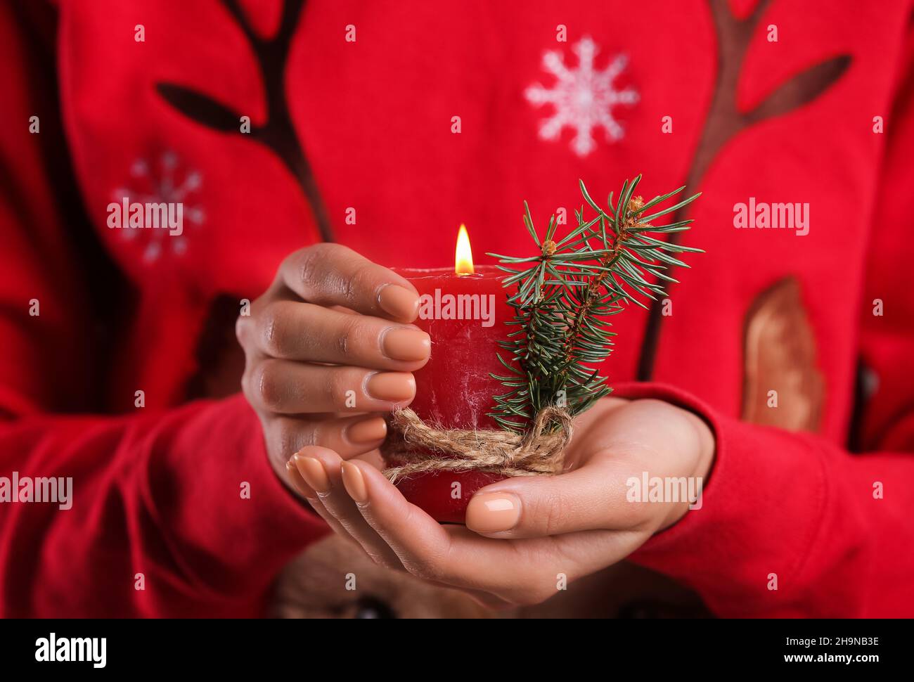 Woman in red sweater holding burning candle with fir branches, closeup ...
