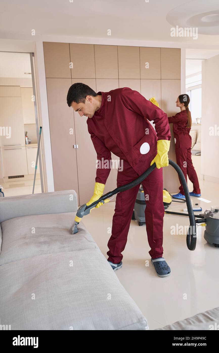 Skilled uniformed janitorial staff cleaning living room Stock Photo - Alamy