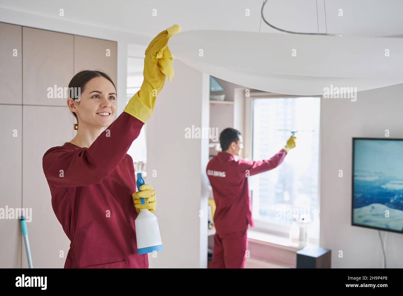 Joyous female cleaner and her colleague cleaning living room Stock ...