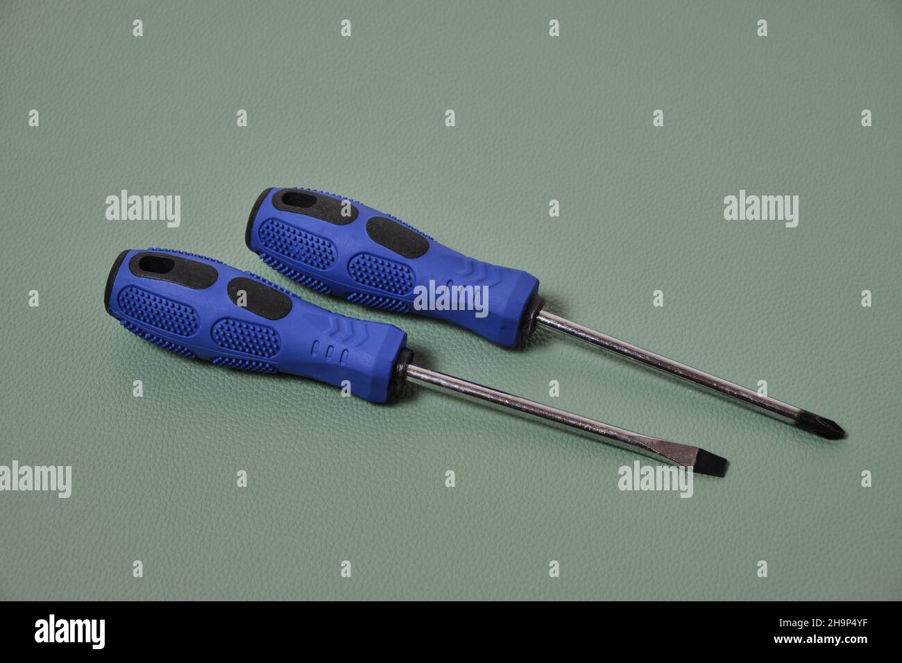 Two screwdrivers cross and flat with blue handles on a green background ...