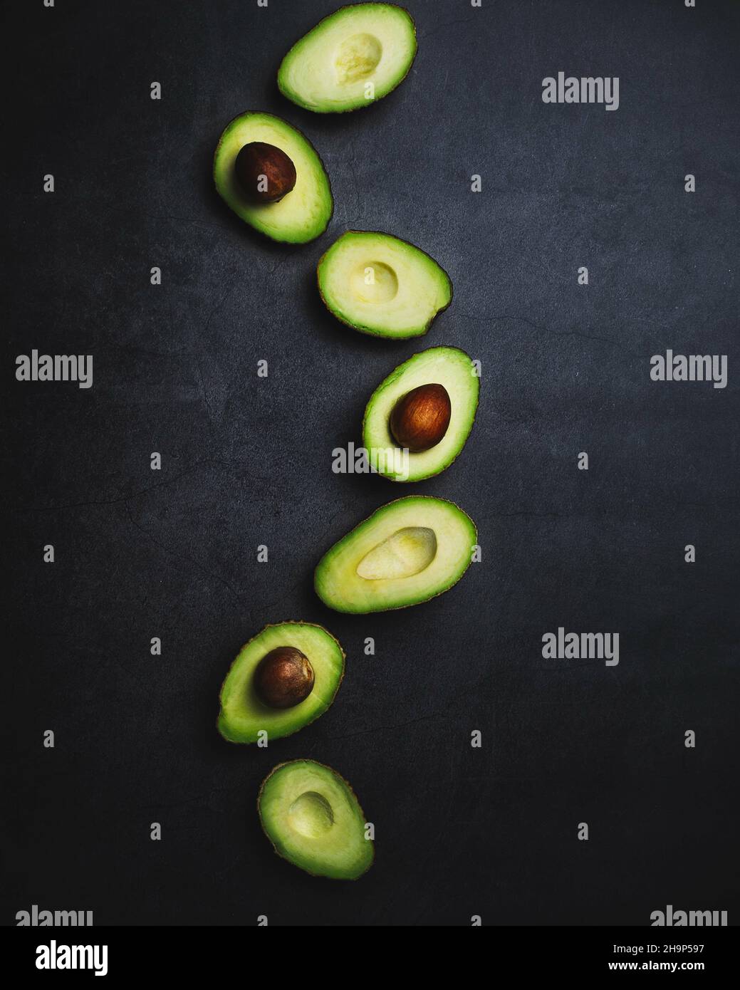 Vertical top view of half avocados in a wavy row on a black background ...