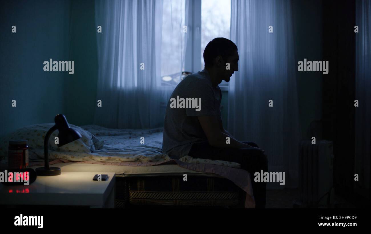 Lonely man sitting on a bed in the dark. Concept of loneliness and ...