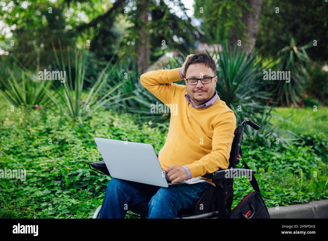a man with disabilities in a wheelchair works on a laptop remotely ...