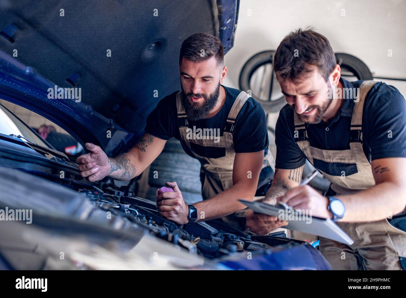 Young auto mechanics changing oil while repairing car engine in a ...