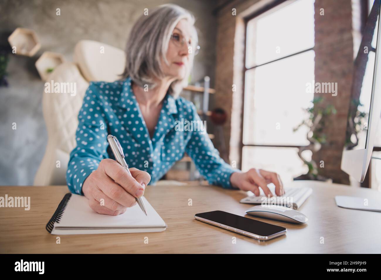Photo of serious old woman write in notebook work businesswoman focused ...