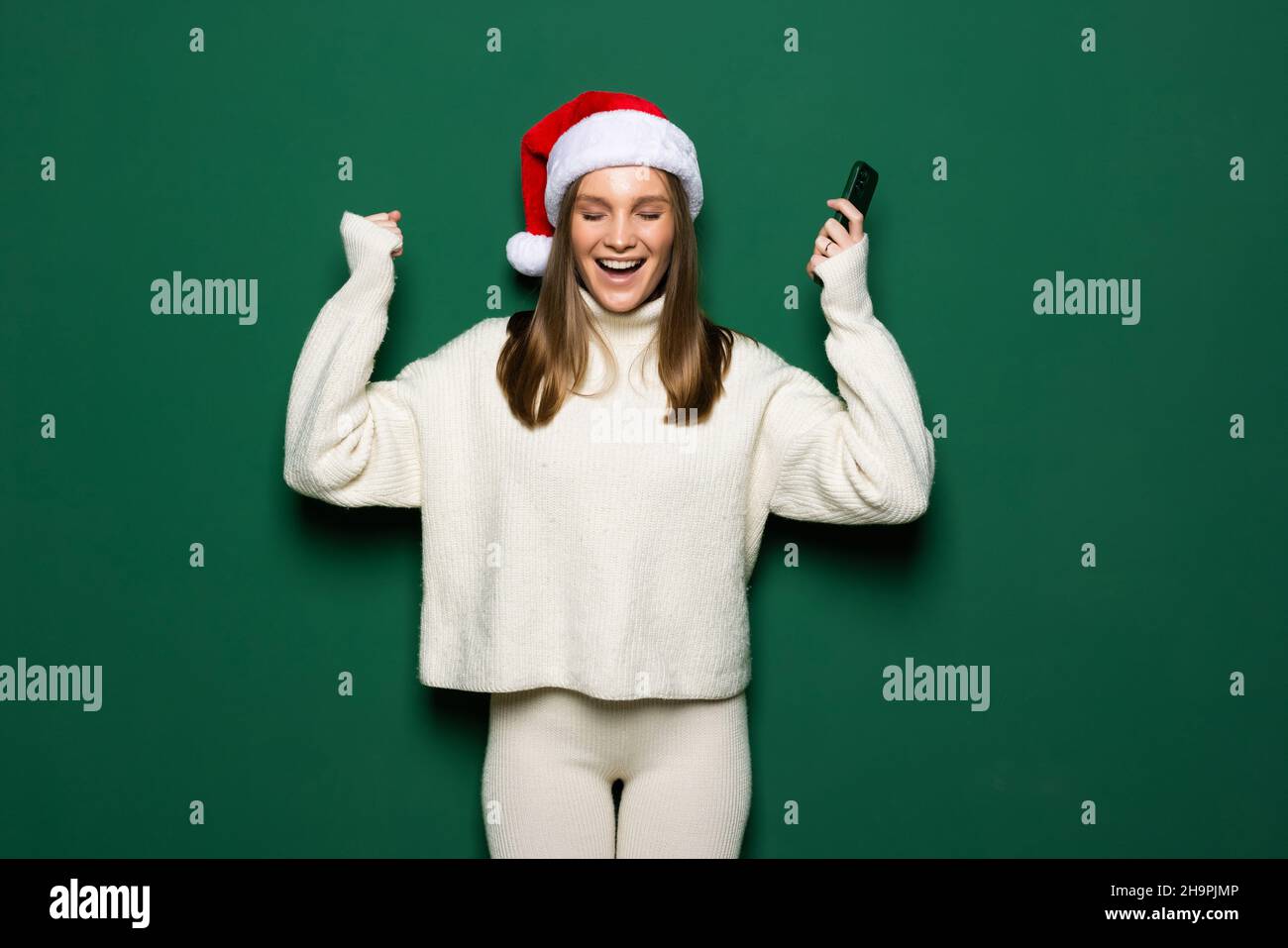 Nice excited girl in Santa Claus hat making winner gesture and using ...