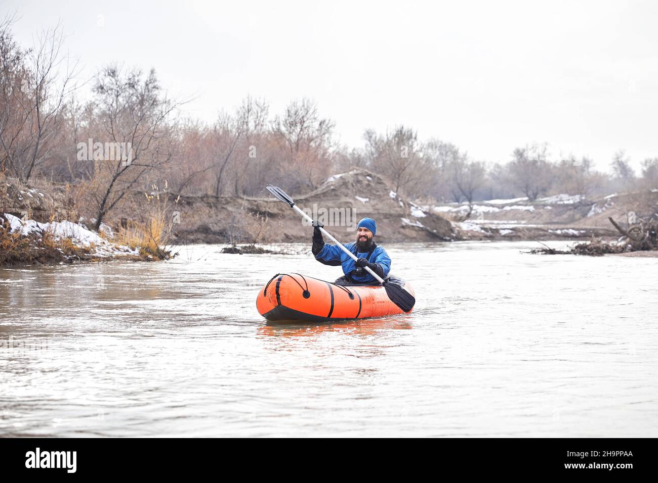 Old man with beard in blue jacket is paddling on orange raft sport boat ...