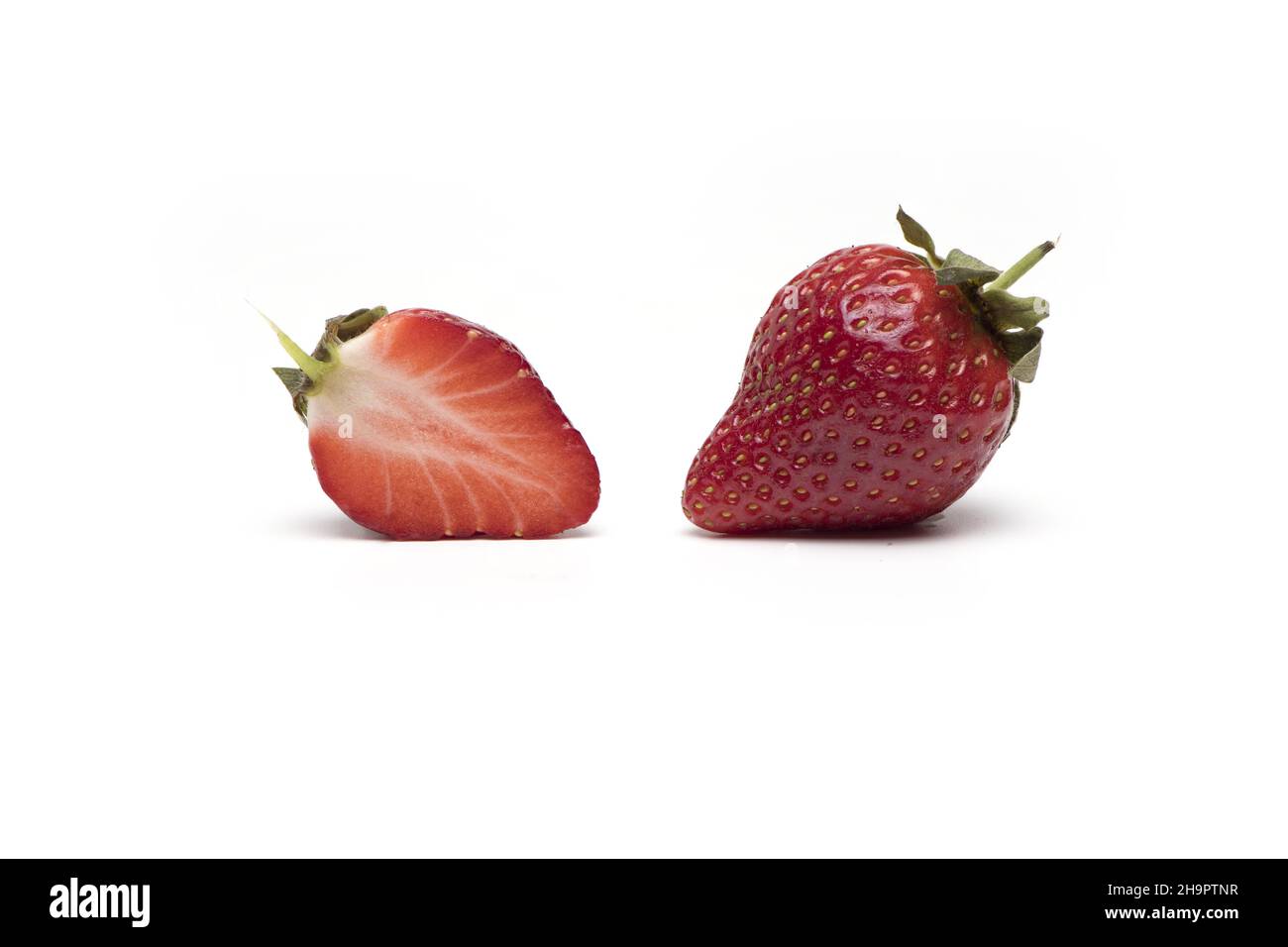 Close up of a whole and a half of a strawberry with green leaves and ...
