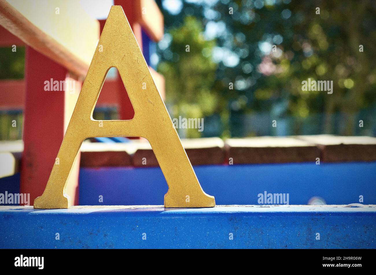 Closeup of a big yellow uppercase A letter in the park with the trees ...