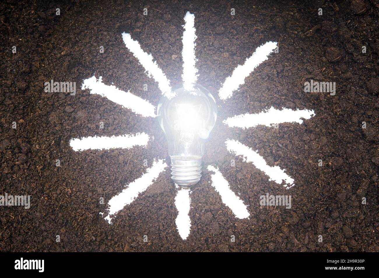 Glowing light bulb with light rays on a soil background. Solar energy ...