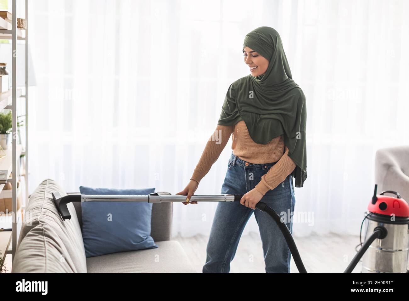 Cheerful muslim woman cleaning couch with vacuum cleaner Stock Photo ...
