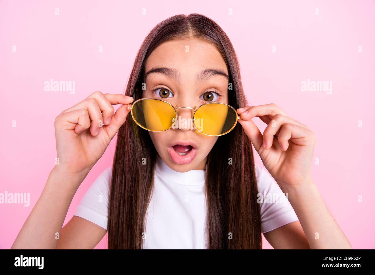 Photo of amazed shocked astonished young little girl hold hands wear sunglass isolated on pink ...