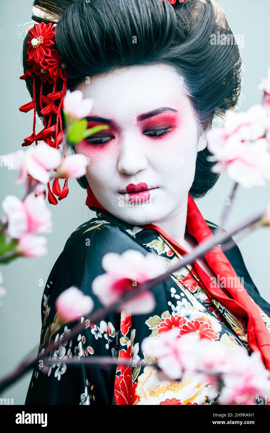 young pretty geisha in black kimono among sakura, asian ethno close up ...