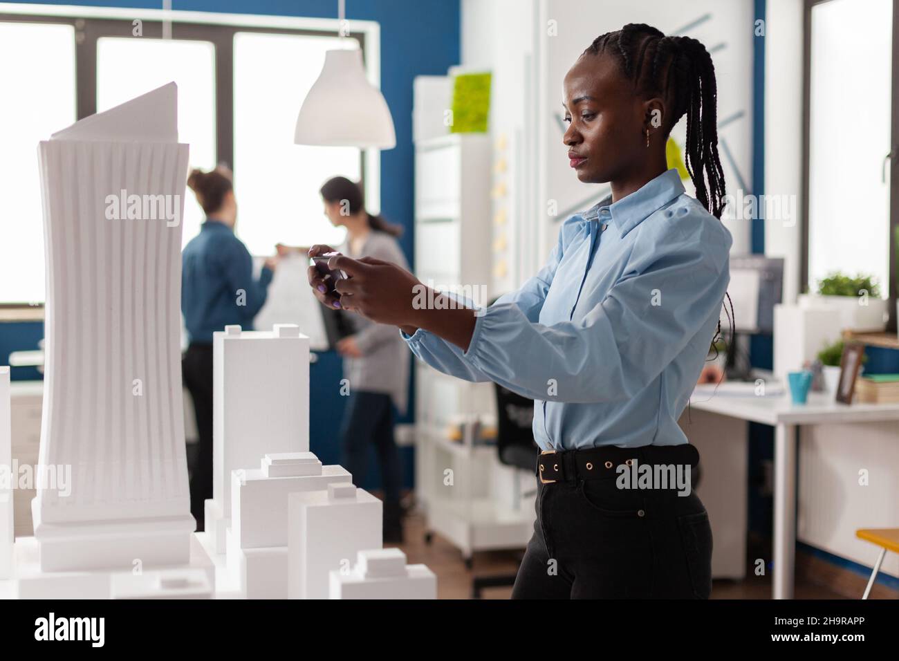 Architect Holding Smartphone In Front Of White Foam Building Model In Modern Architectural