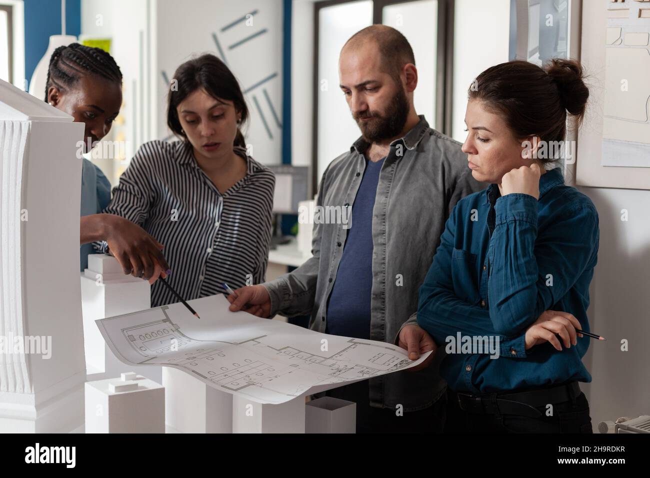 Team Of Architects Analyzing Blueprints For Building Project Standing In Front Of Table With