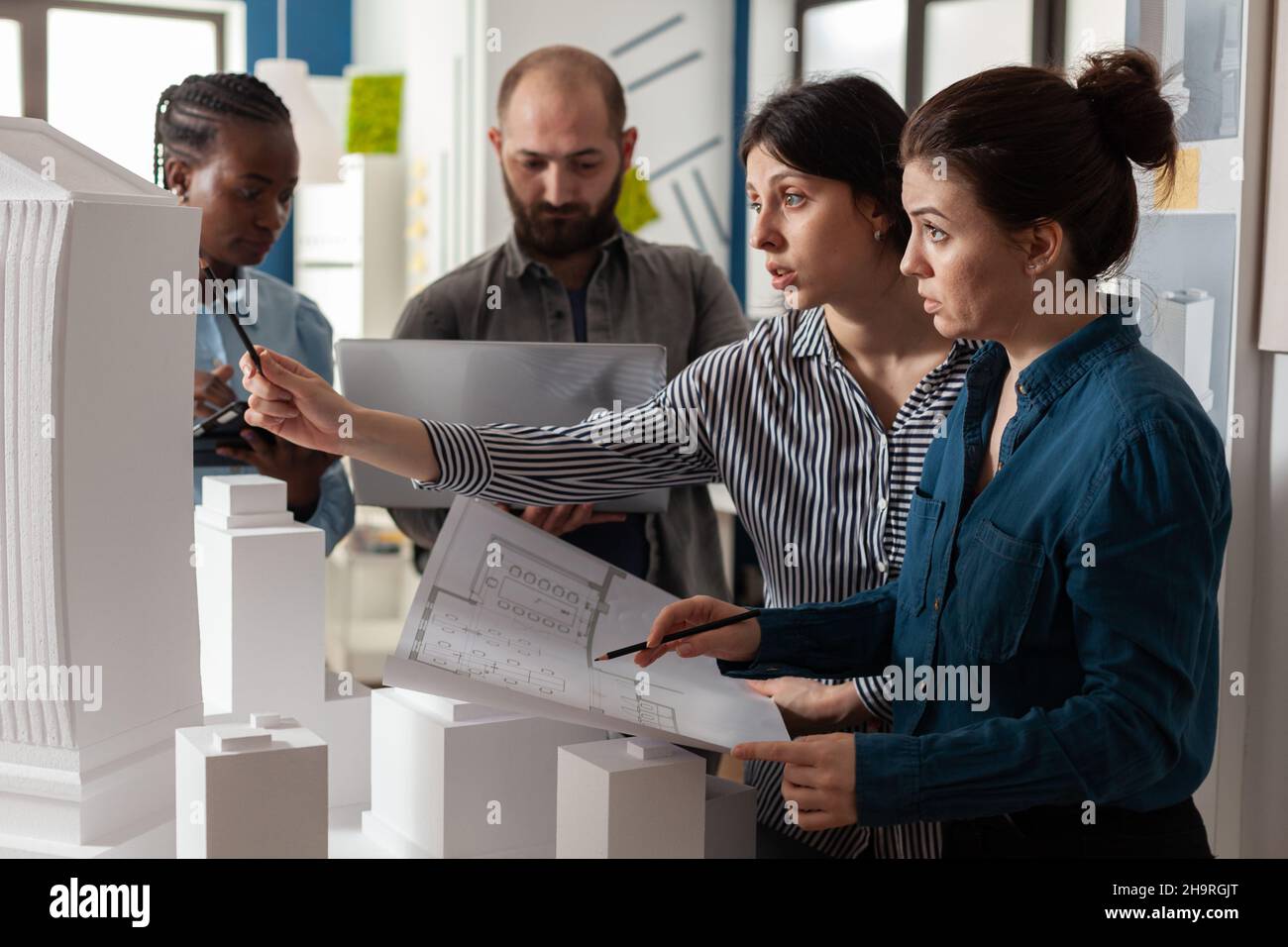 Two women professional architects holding blueprints next to colleagues ...