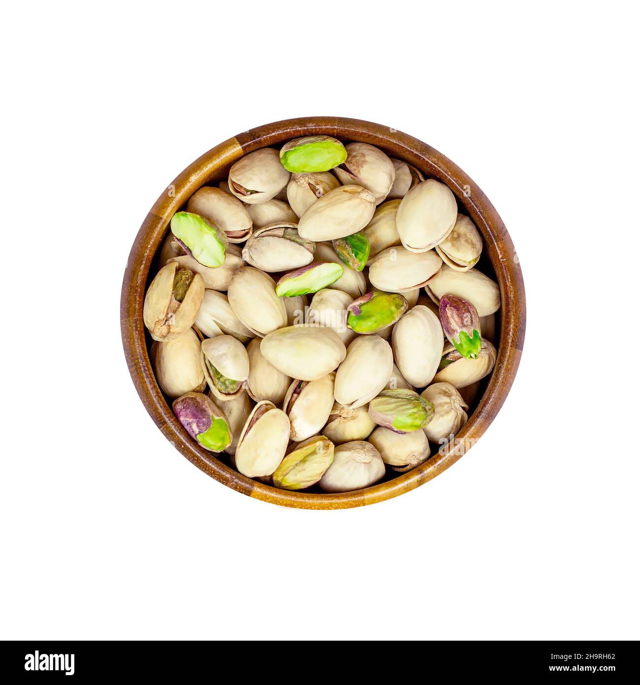 Top view of roasted salted pistachio nuts in nutshell in the round brown wooden bowl isolated on ...