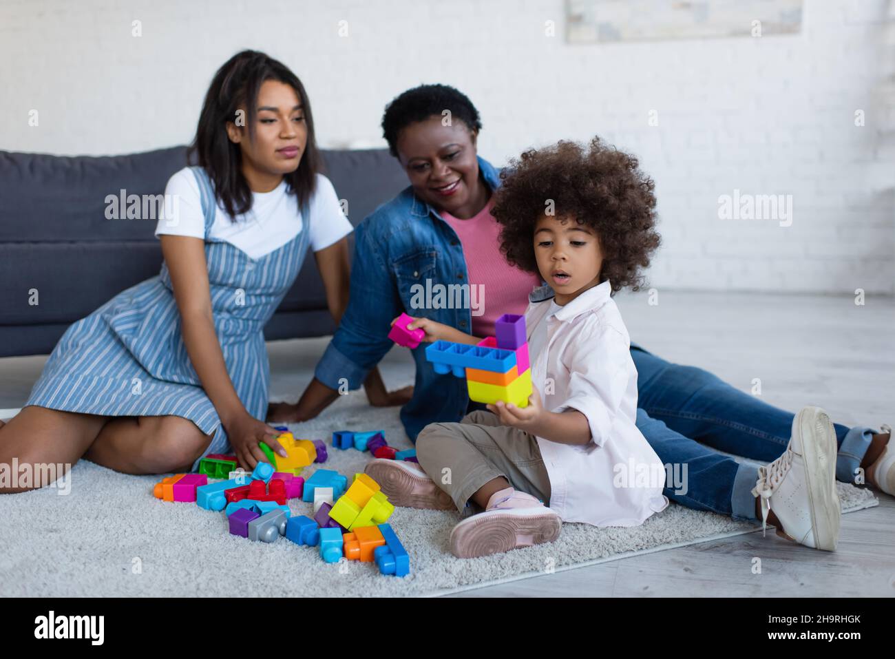 happy african american women looking at girl playing with building ...