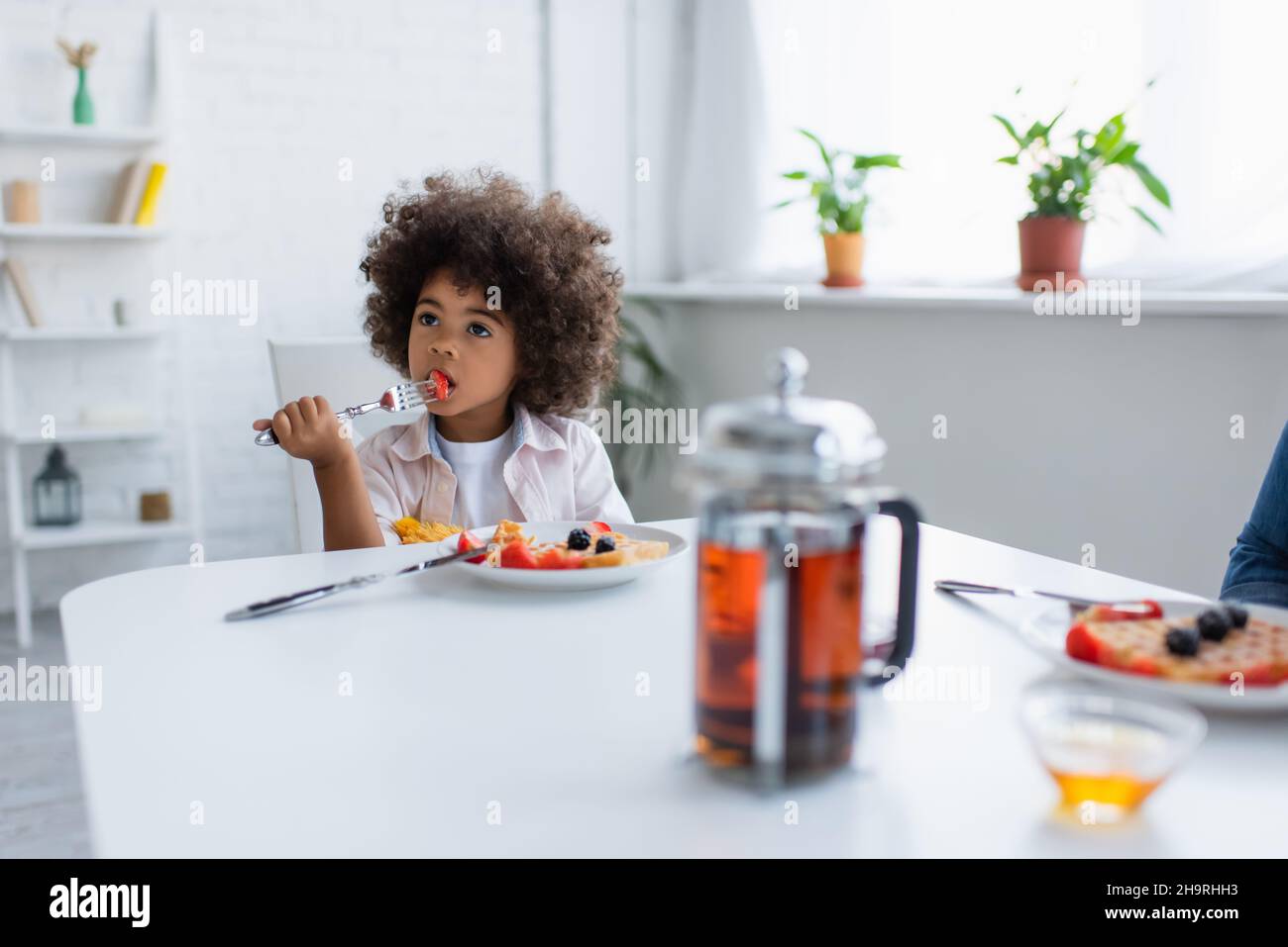 african american girl having breakfast near blurred teapot on kitchen ...
