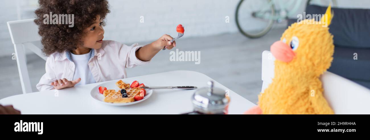 african american child proposing strawberry to toy chick during ...