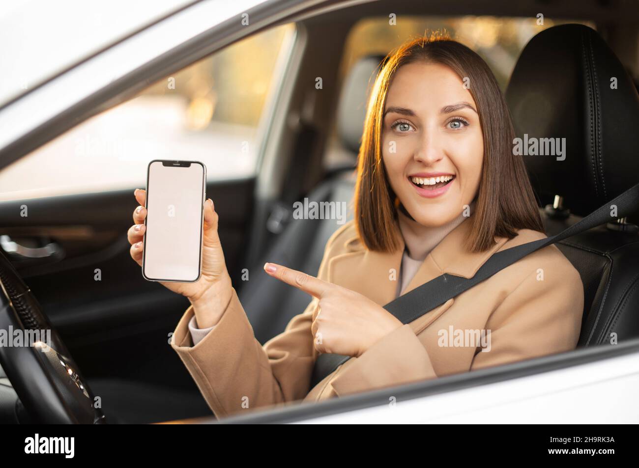 Young beautiful surprised woman driving a car, female points to blank ...