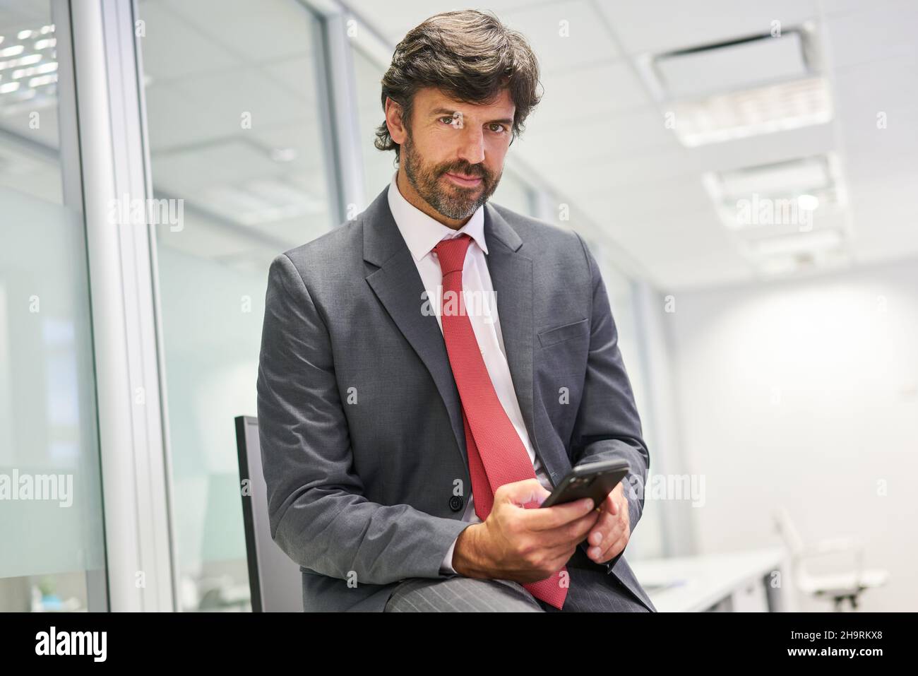 Successful man as senior business manager sitting with smartphone in ...