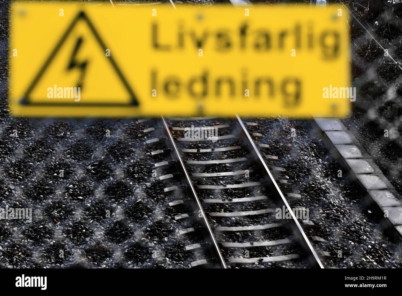 Defocused fence and warning sign in front of rail track. The sign says ...