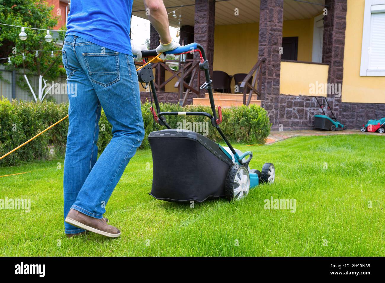 A man mowing a lawn with an electric mower in the garden backyard Stock ...