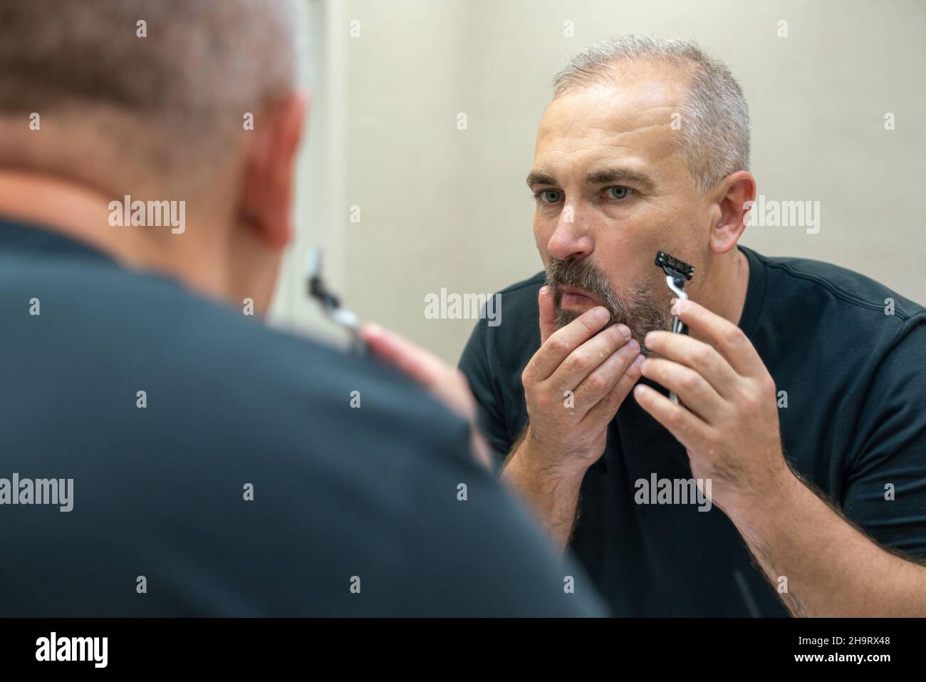 Charming middle aged man shaving his beard and moustache off in front ...