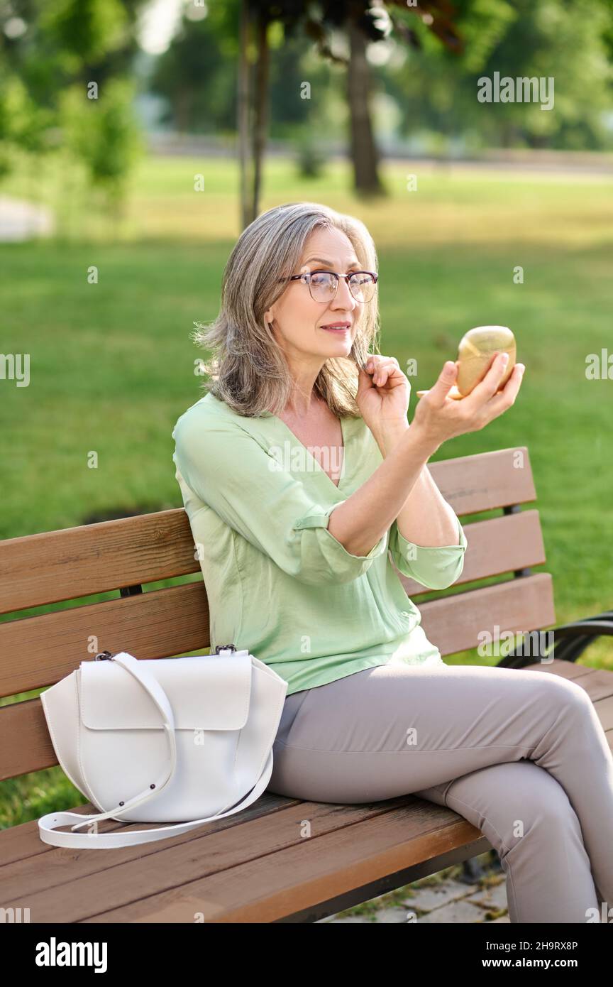Woman looking in mirror sitting on bench Stock Photo - Alamy