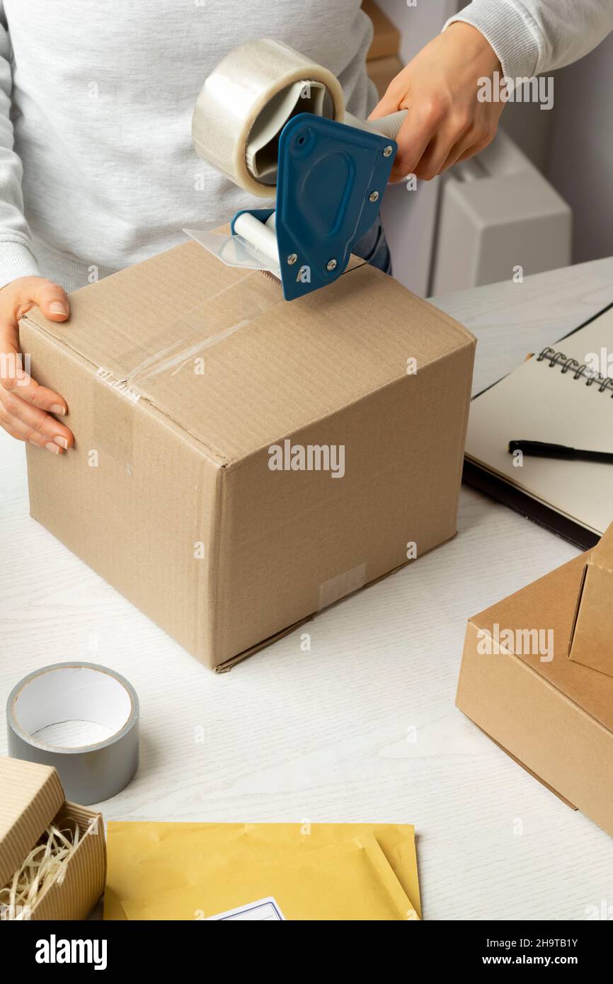 A warehouse worker packs a cardboard box with a tape dispenser Stock ...