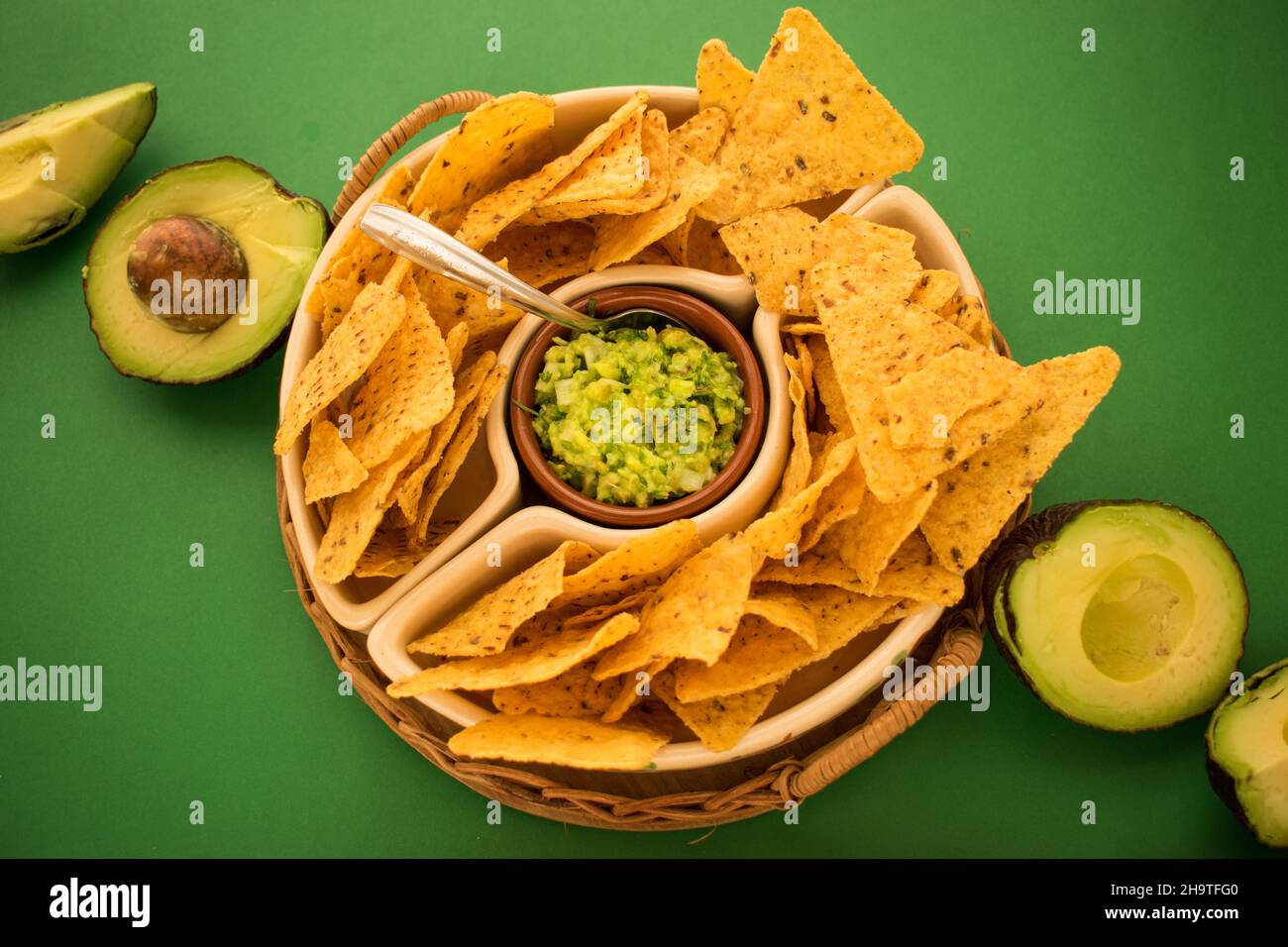 Some fried nachos in a pot with some fresh guacamole on a green surface ...