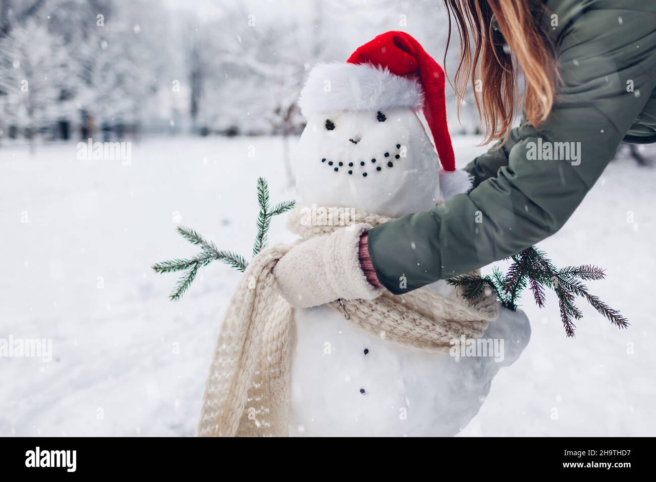 Girl makes snowman outdoors in snowy winter park dressing it in Santa ...